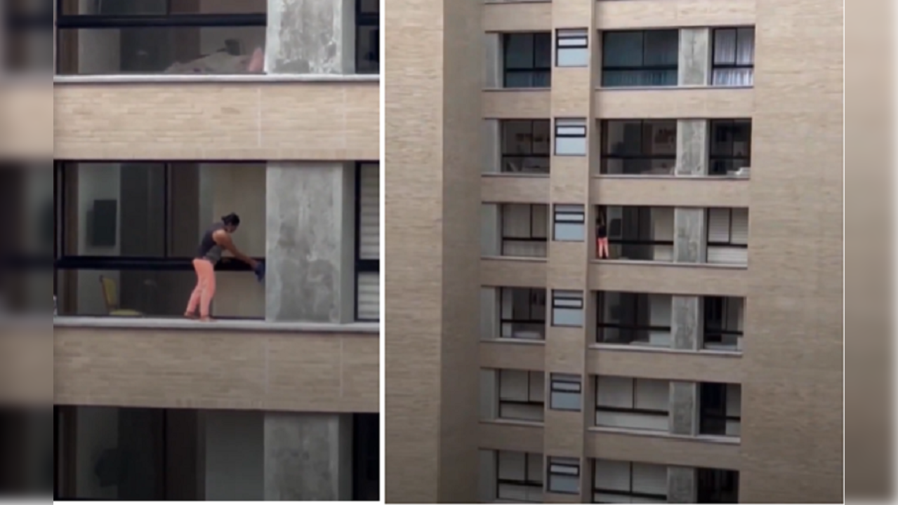 Woman cleans windows of her high-rise apartment, standing on ledge ...